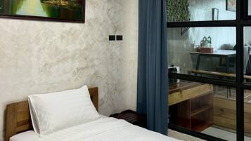 Quarto com cama, janela com vista para uma área de refeições e um quadro na parede.