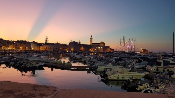 Uma marina com barcos atracados, uma torre imponente e edifícios à beira-mar.