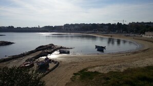 Uma praia com barcos, uma faixa de areia e edifícios ao fundo.