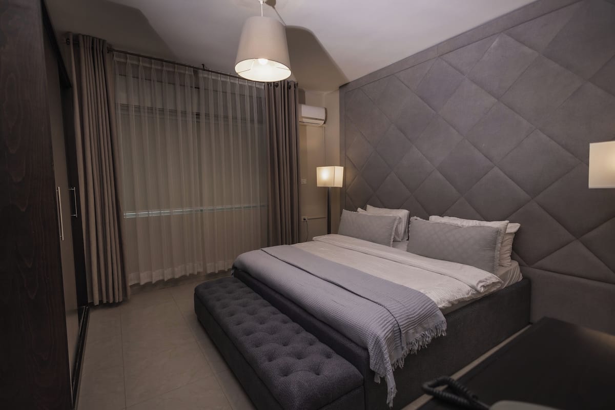 Quarto moderno com uma cama grande, um banquinho, uma luminária pendente e um ar condicionado fixado na parede.