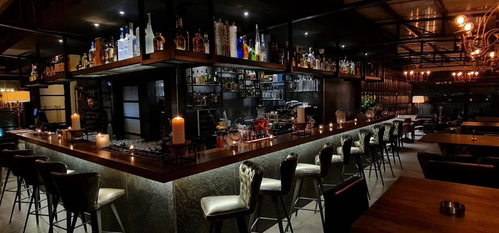 Uma área de bar com balcão comprido, banquetas e prateleiras cheias de garrafas.