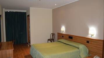 Quarto de hotel com uma cama, uma cadeira, uma escrivaninha e um telefone.