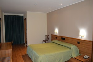 Quarto de hotel com uma cama, uma cadeira, uma escrivaninha e um telefone.