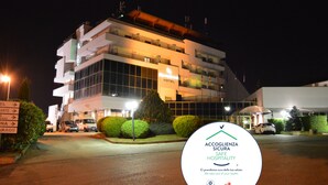 Um hotel de vários andares com design moderno, destacando uma placa com a inscrição Accoglienza Scuria Safe Hospitality.