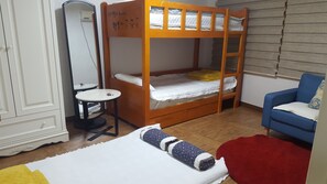 Uma cama beliche com uma mesinha e cadeira, um espelho e um tapete vermelho num quarto com piso de madeira.