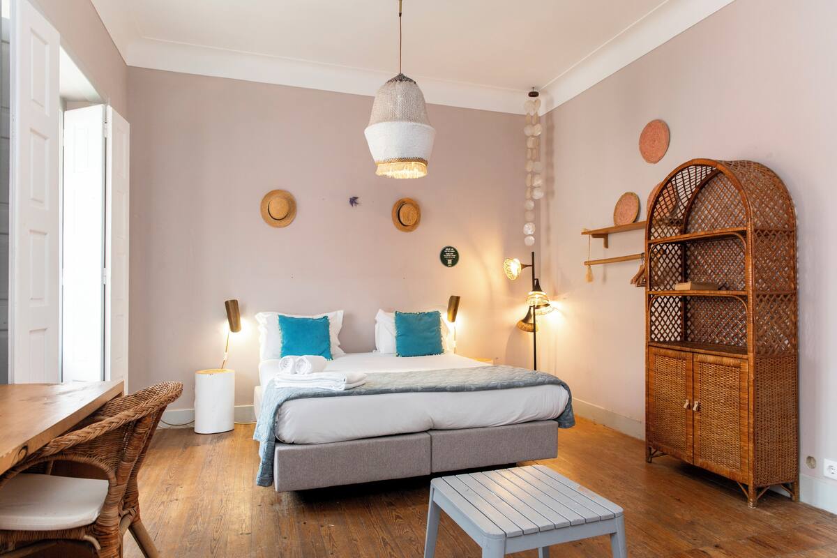 Quarto com cama, luminárias de cabeceira, um armário de vime e chão de madeira.