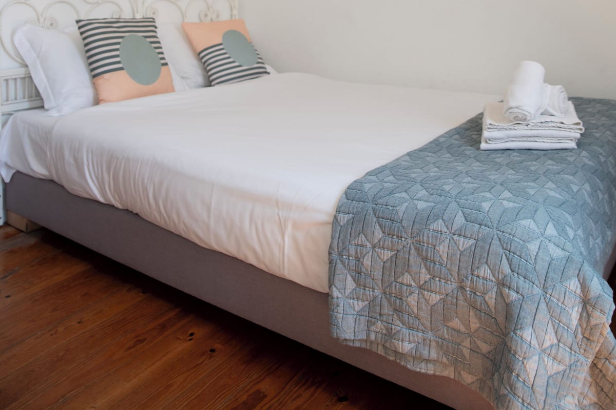 Cama bem arrumada com manta estampada, cabeceira decorativa e luminária pendente.