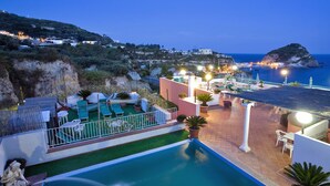 Piscina no terraço com vista para o mar e uma cidade ao longe.