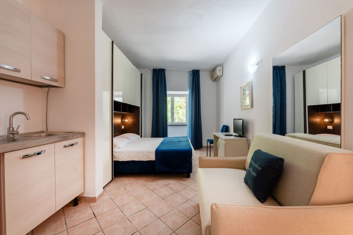 Quarto de hotel com cama, sofá, escrivaninha, espelho e janela com cortinas.