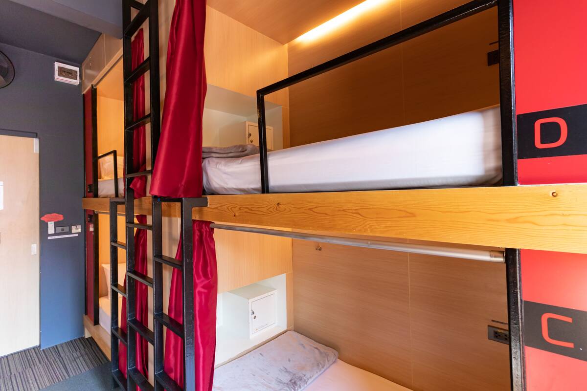 Quarto com beliche de madeira, uma pequena escrivaninha e cortina vermelha.