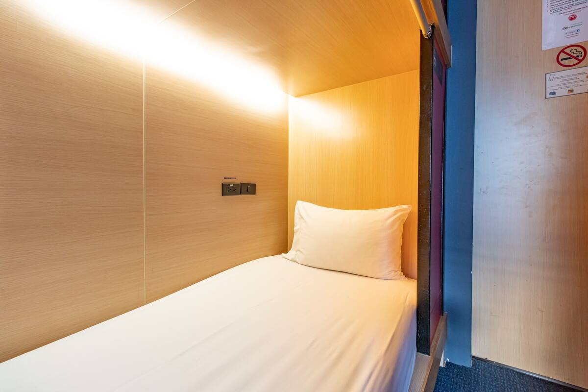 Uma cama de solteiro num quarto com paredes de madeira e uma porta à direita.