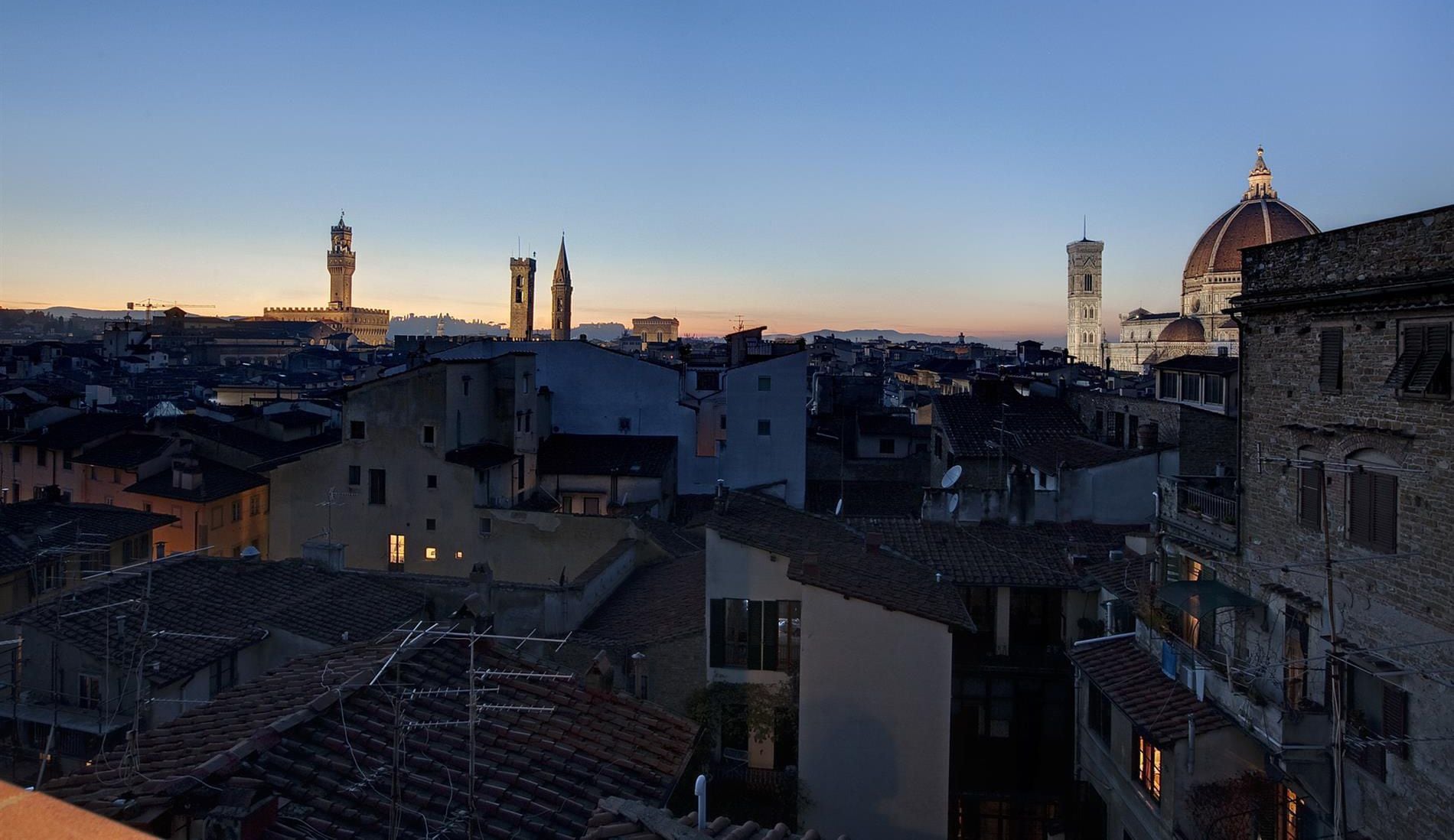 Paisagem urbana com edifícios históricos, incluindo uma torre de sino imponente e uma estrutura em cúpula, sugerindo um cenário europeu.