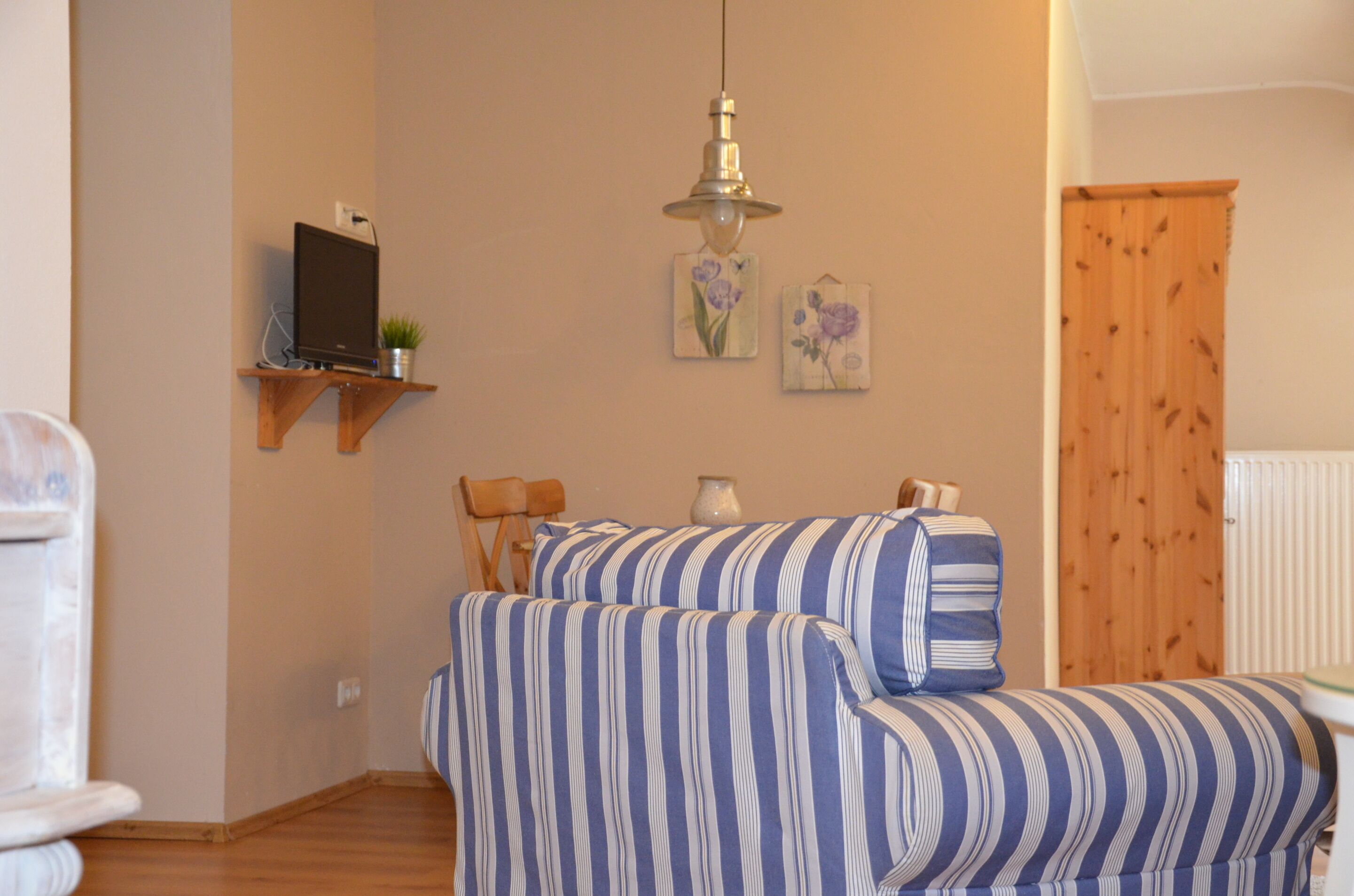 Um quarto com um sofá listrado, uma mesinha, uma luminária pendente e uma estante fixada na parede com uma planta e um quadro.