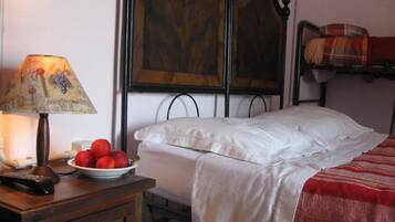 Quarto com cama, mesa de cabeceira com abajur, uma tigela de frutas e um quadro na parede.