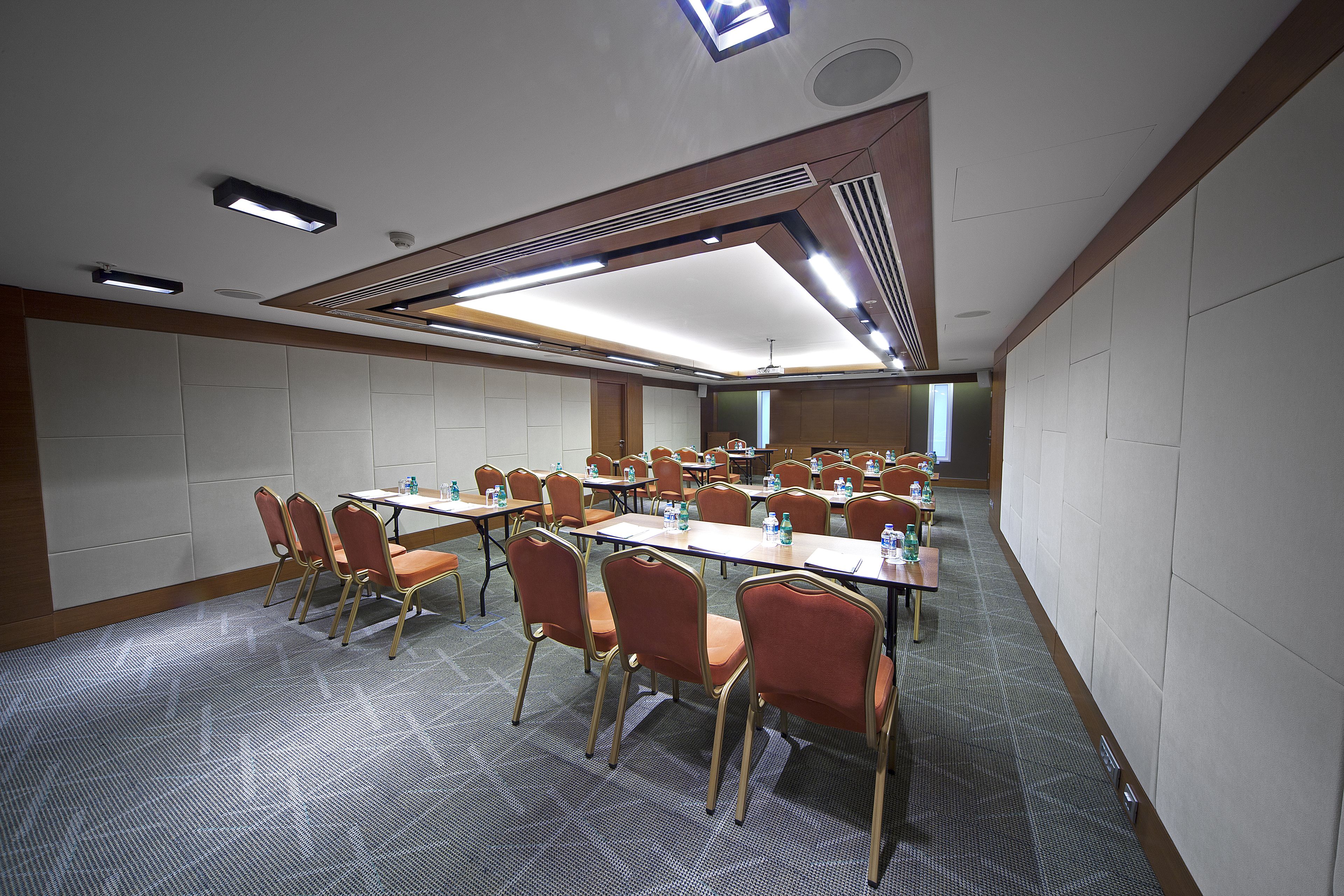Sala de conferência com várias mesas e cadeiras, equipada com garrafas de água e blocos de anotações.