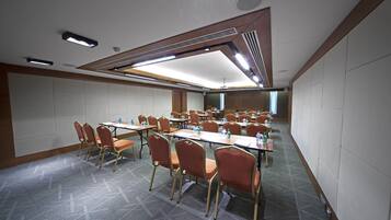 Sala de conferência com várias mesas e cadeiras, equipada com garrafas de água e blocos de anotações.