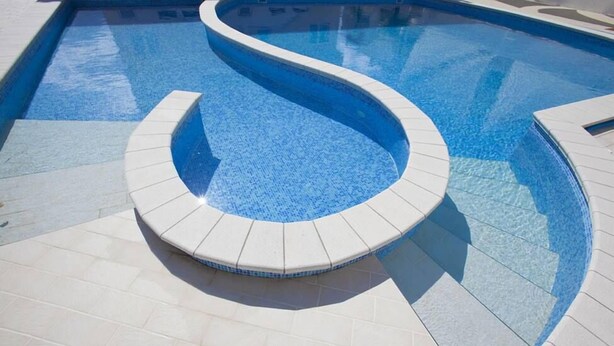 Piscina com design curvo singular e um deck revestido ao redor.