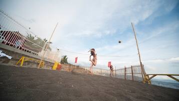 Uma quadra de voleibol de praia com rede, superfície arenosa e cerca de madeira.