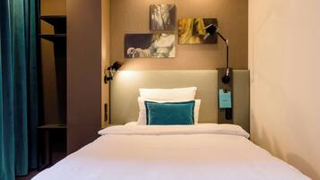 Quarto de hotel com cama, mesa de cabeceira, abajur e obras de arte na parede.