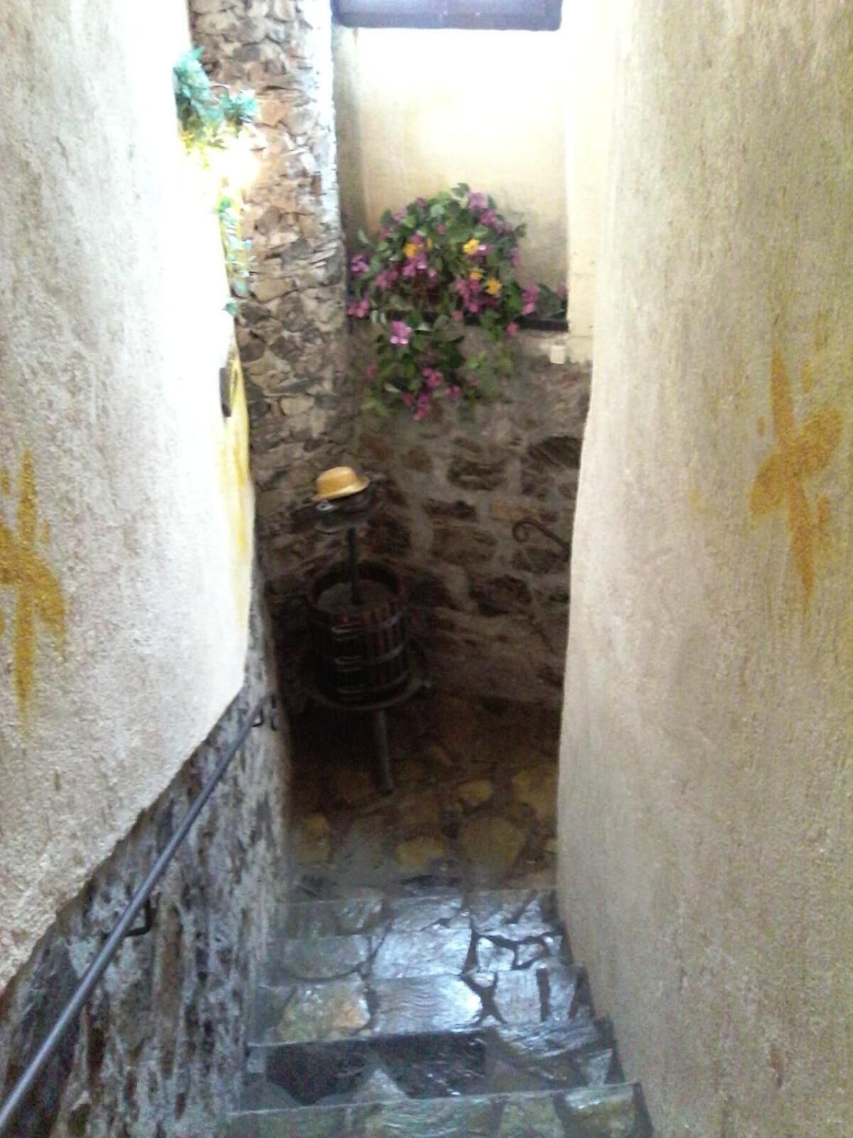 Uma escadaria de pedra estreita com corrimão de metal, conduzindo a um pequeno quarto com parede de pedra e uma janela.