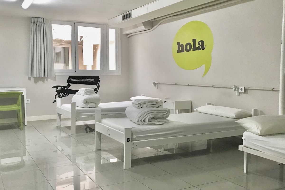 Quarto de hotel com duas camas, uma escrivaninha, uma cadeira e uma janela com cortinas.