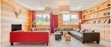 Sala moderna com paredes de madeira, um sofá vermelho, um sofá cinza e uma TV à esquerda.