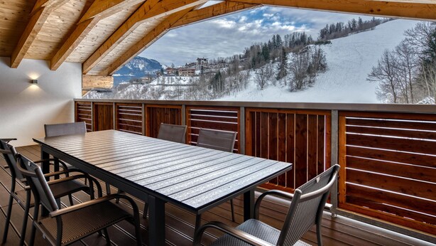 Um deck de madeira com mesa e cadeiras, com vista para uma paisagem montanhosa coberta de neve.