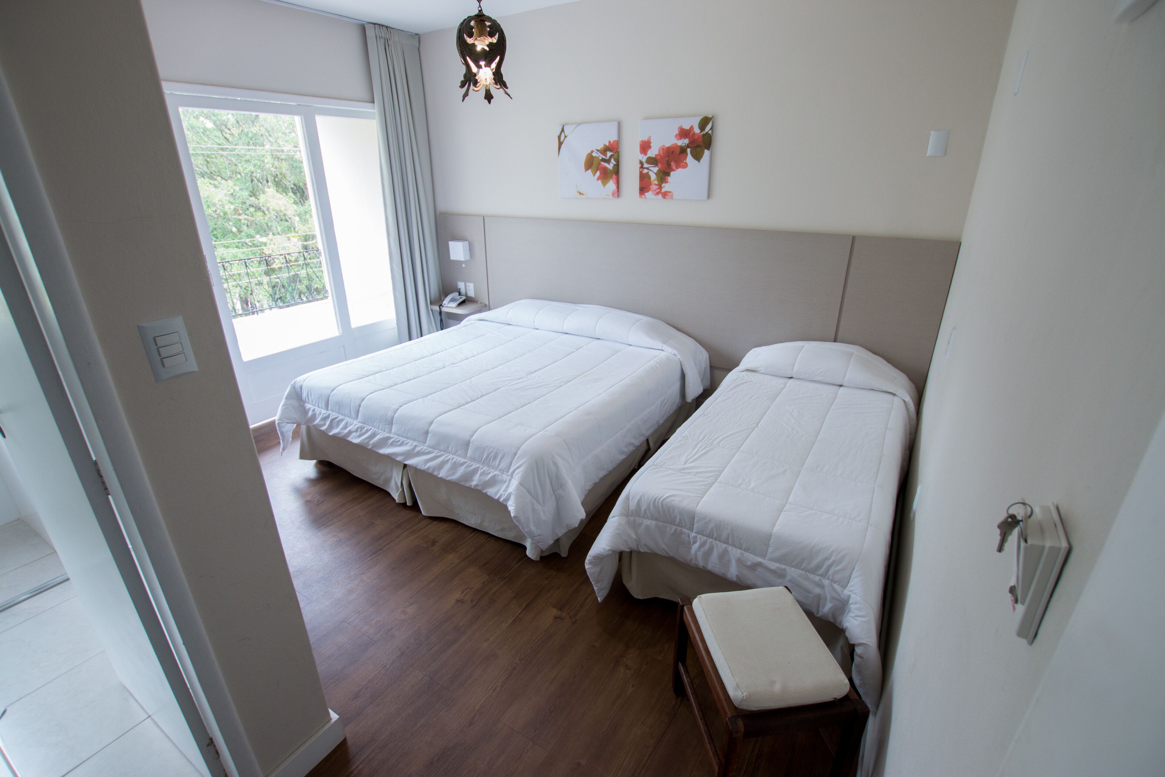 Quarto com duas camas, uma mesinha de cabeceira e uma janela com cortinas.