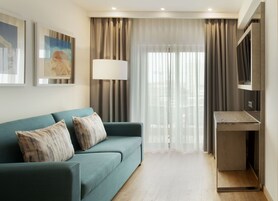 Uma sala de estar moderna com um sofá verde-turquesa, um abajur e uma TV em um suporte.