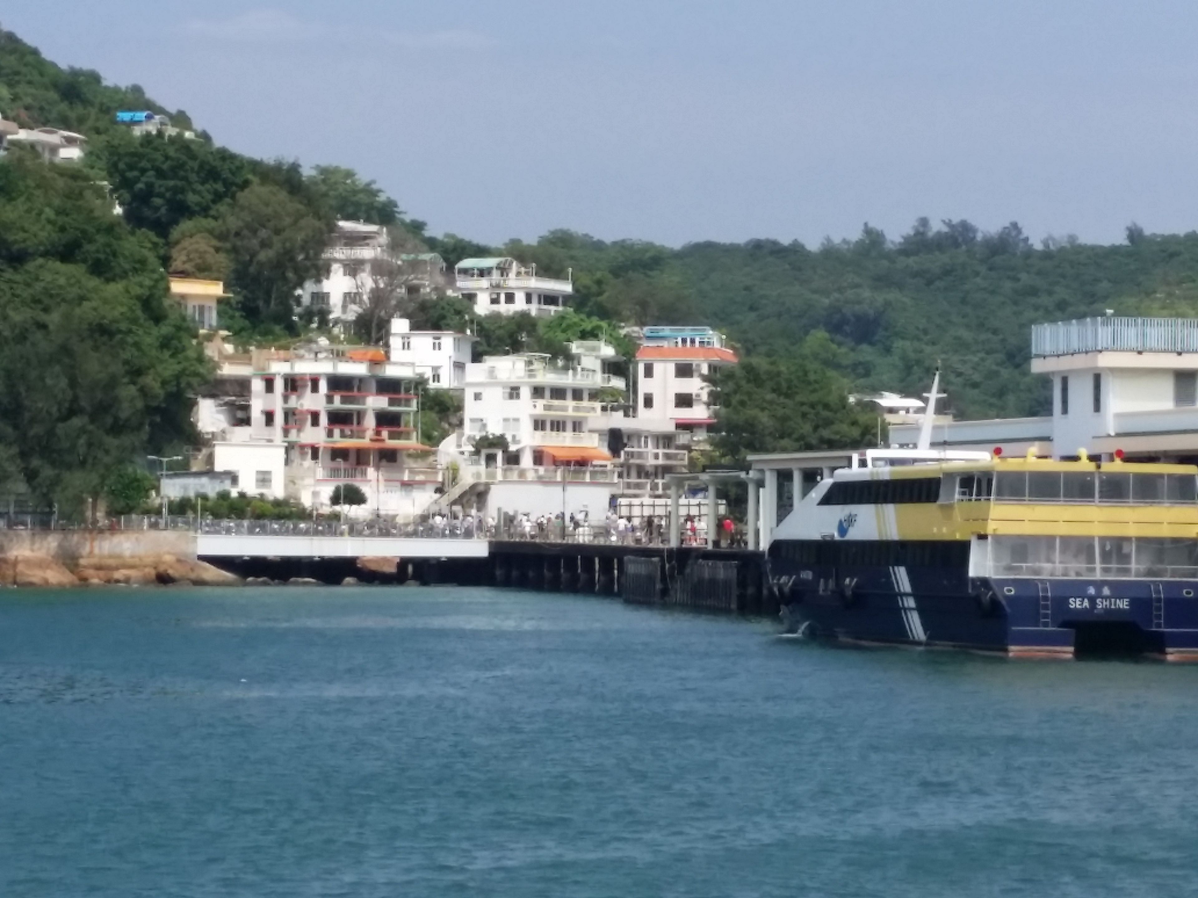 Um ferry atracado em um cais, com prédios altos e uma encosta ao fundo.