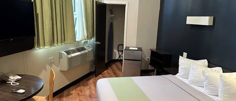 Quarto de hotel com cama, escrivaninha com cadeira, televisão, ar condicionado e pequeno frigorífico.