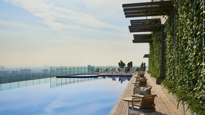 Piscina infinita no terraço com vista para a cidade, deck de madeira e mobiliário de vime.