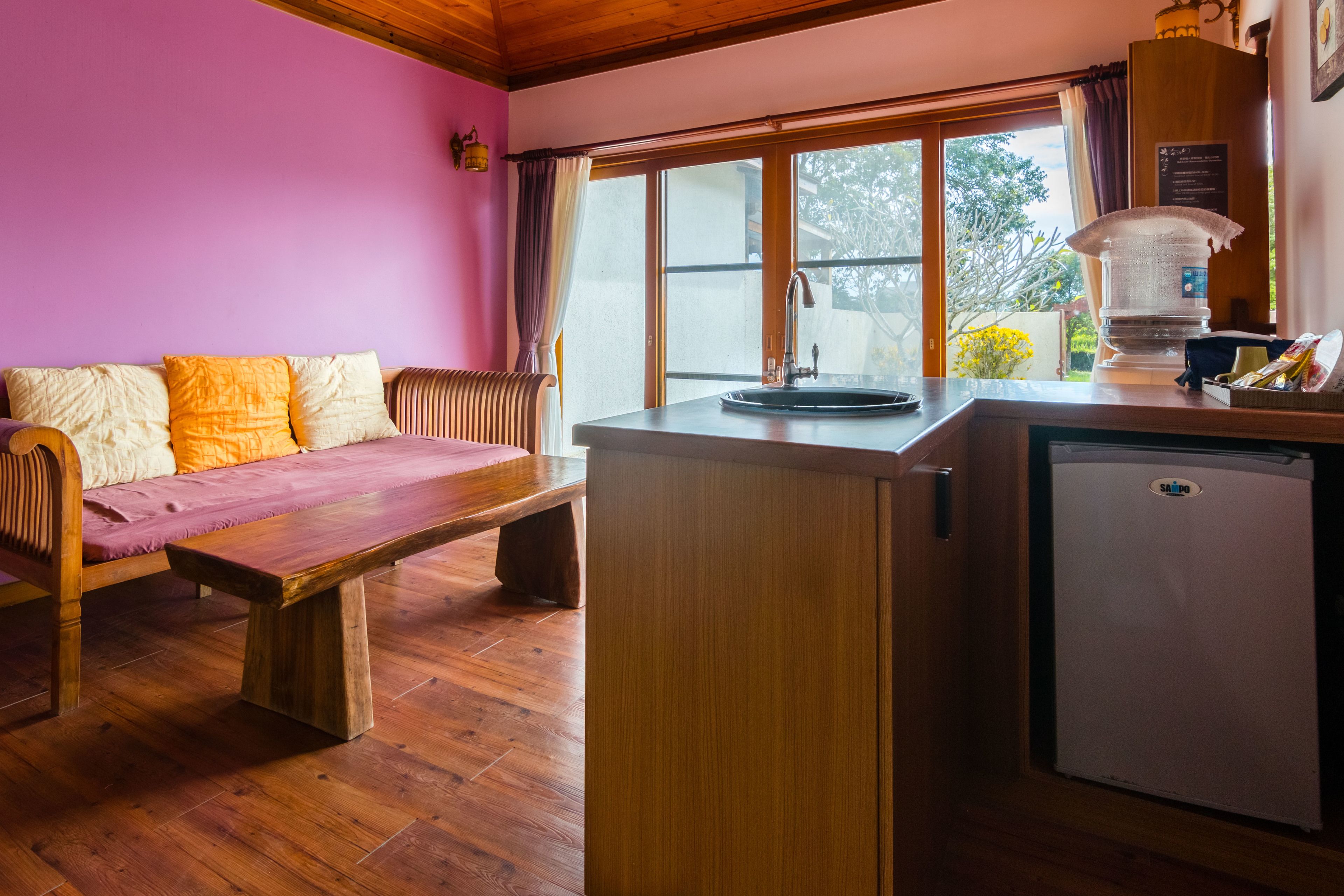 Um quarto acolhedor com um banco de madeira, uma kitchenette pequena e uma janela com vista para o verde.