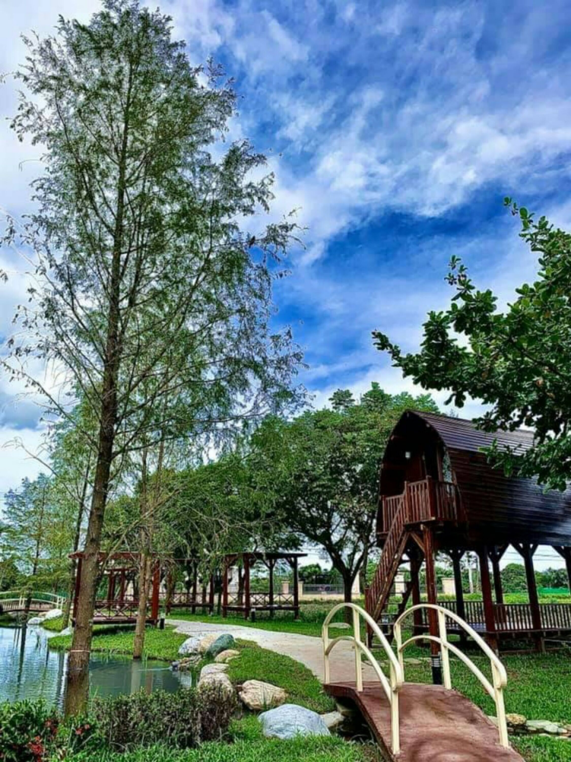 Um gazebo de madeira com galeria coberta, cercado por árvores e um pequeno lago.