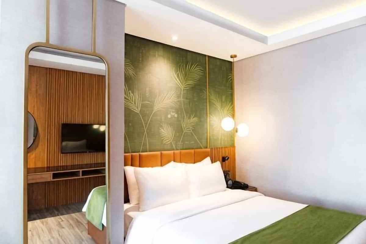 Quarto de hotel moderno com uma cama, uma televisão e um painel decorativo verde.