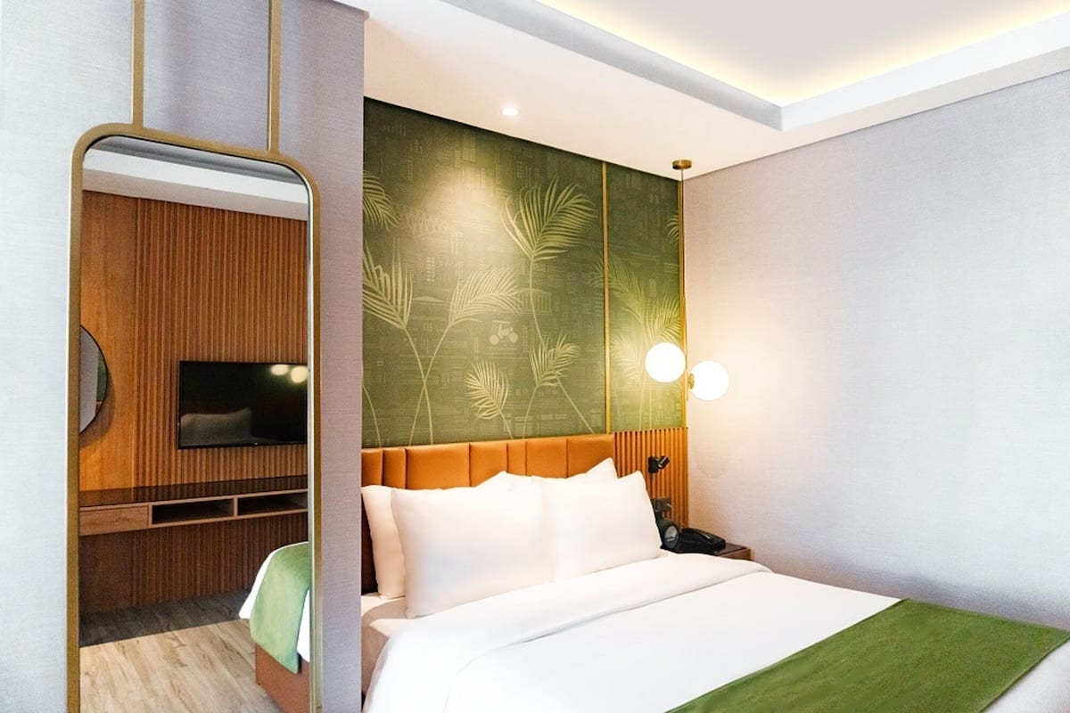 Quarto de hotel com uma cama, uma TV, um espelho e uma parede com um padrão de folhas.