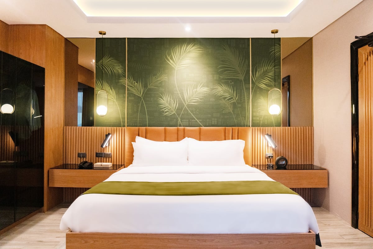 Quarto de hotel moderno com uma cama grande, cabeceira de madeira e espelho fixado na parede.