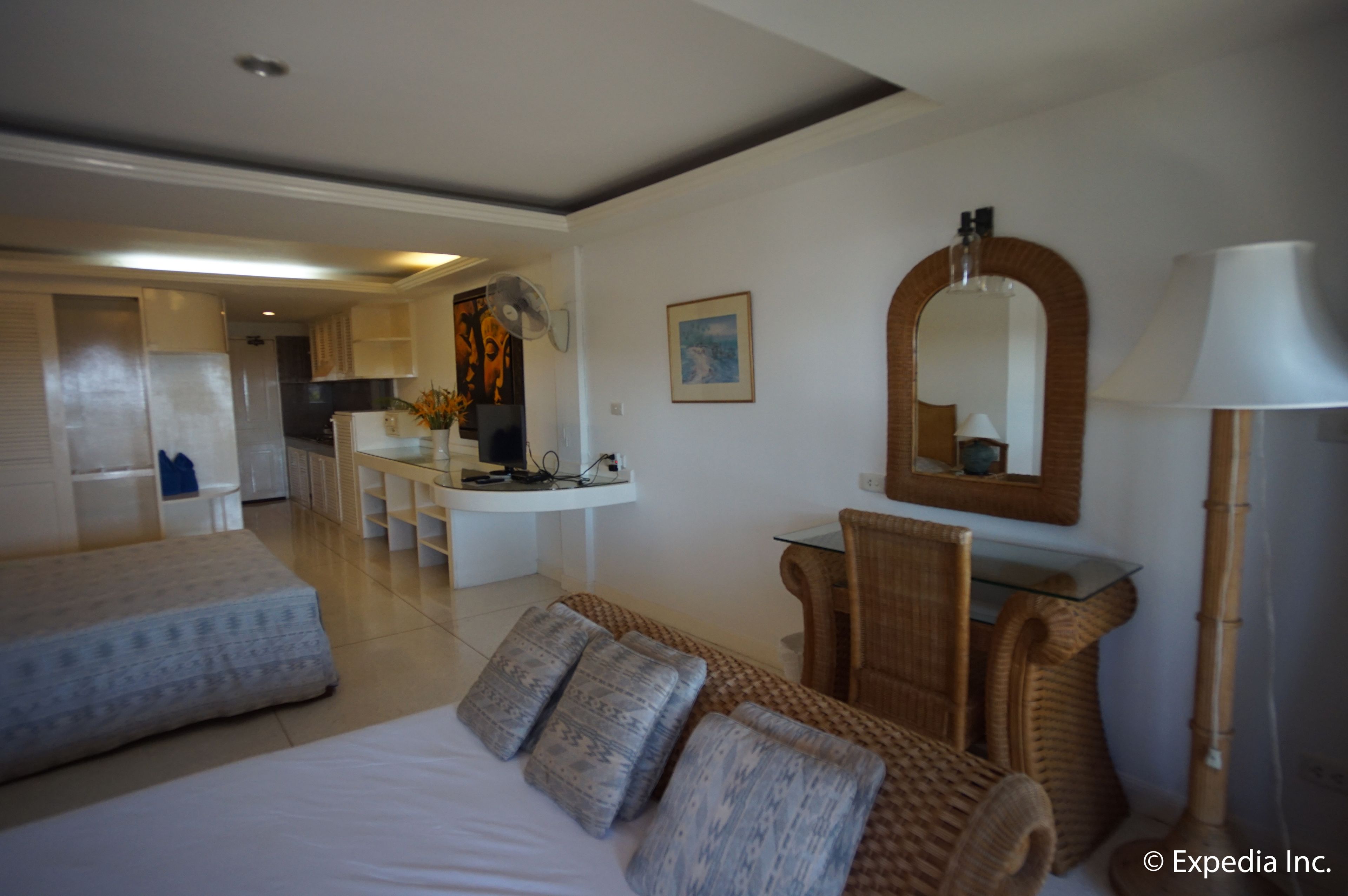 Quarto de hotel com cama, área de estar com poltrona e mesa, cozinha compacta e banheiro.