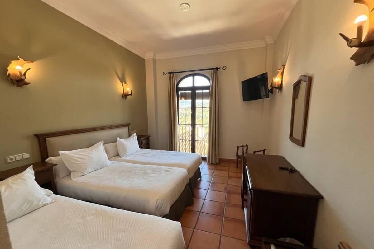 Quarto de hotel com duas camas, uma escrivaninha, televisão na parede e uma janela com cortinas.