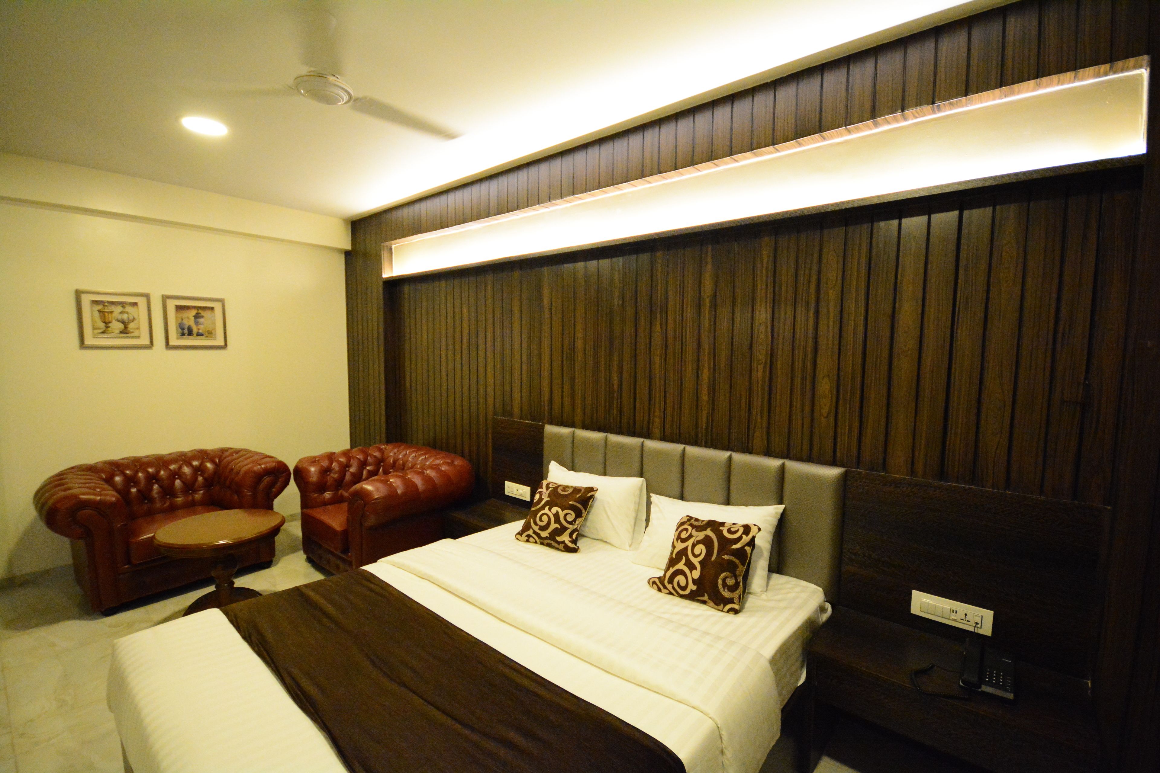 Quarto de hotel com uma cama, duas poltronas de couro, uma mesinha e um painel de cabeceira em madeira.