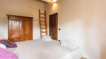 Quarto com cama, guarda-roupa de madeira, escada e porta.