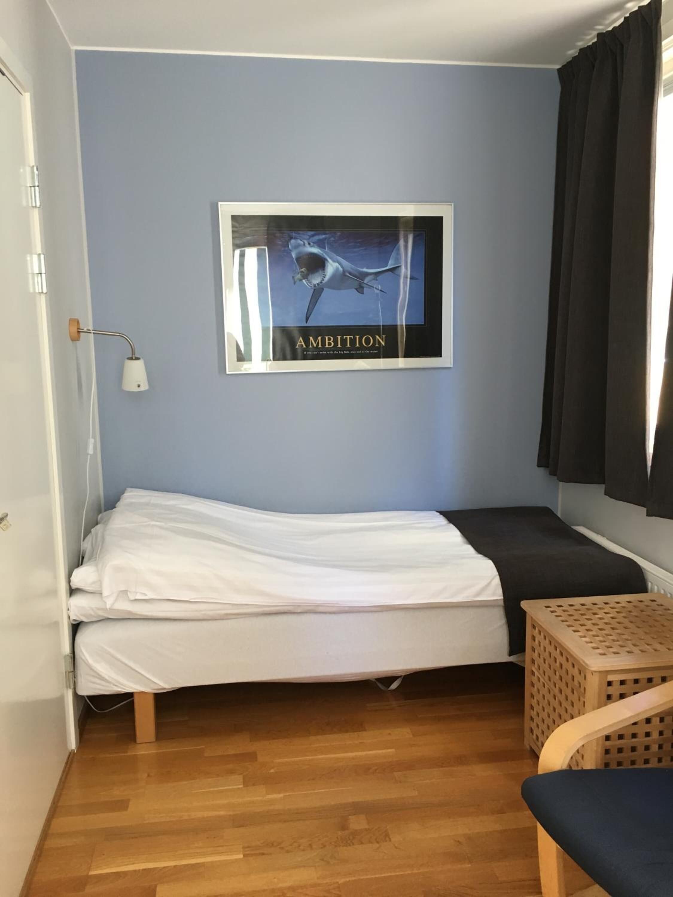 Um quarto pequeno e bem arrumado, com uma cama, uma mesinha e um quadro na parede.