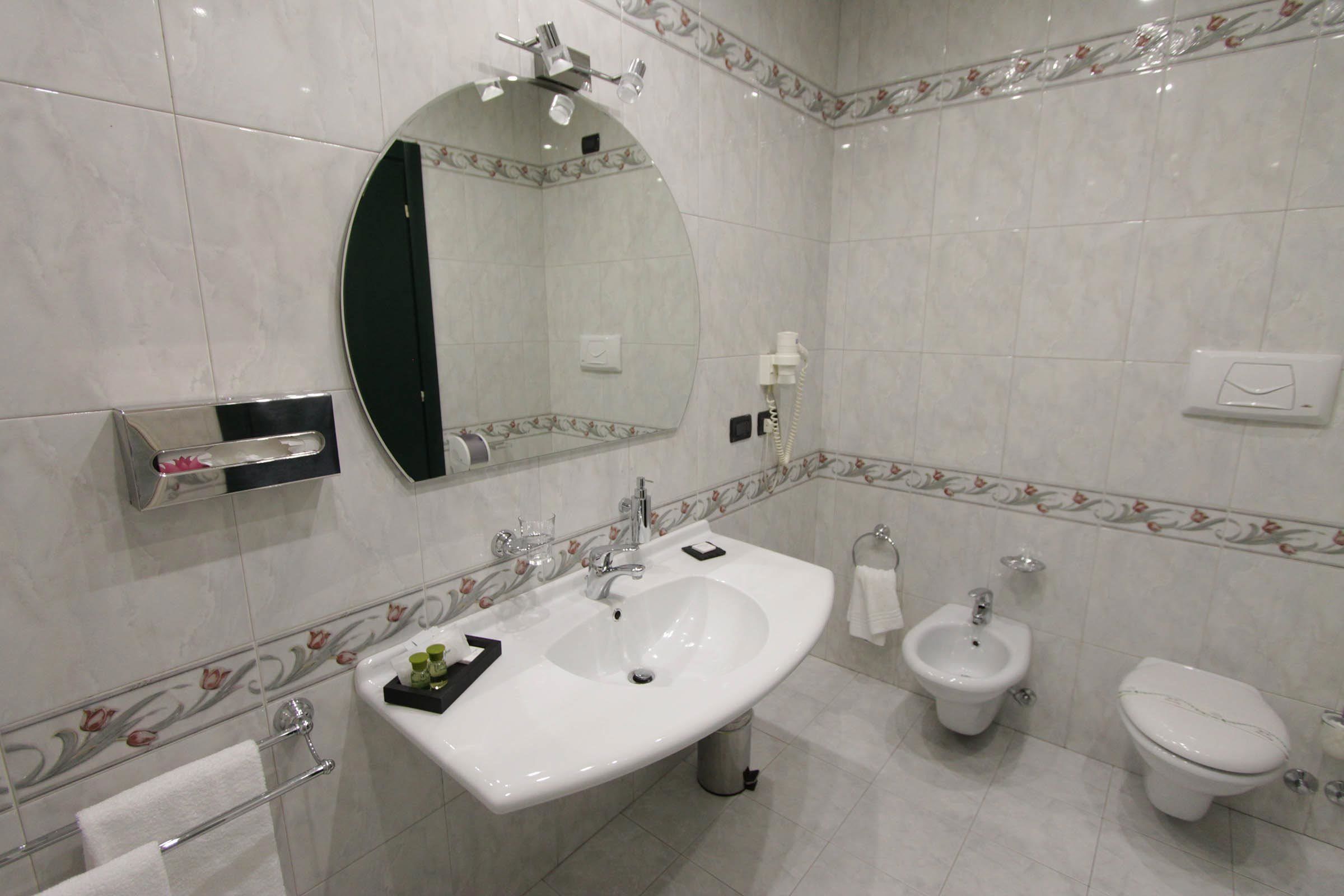 Casa de banho com lavatório branco, bidé, sanita e espelho, com um porta-toalhas.