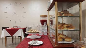 Disposição de buffet de café da manhã, com um relógio, mesas e uma vitrine de vidro com doces.