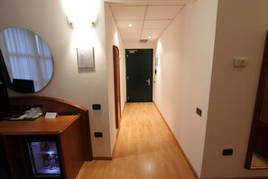 Um corredor de hotel com uma mesa de recepção, um espelho e uma porta no final.