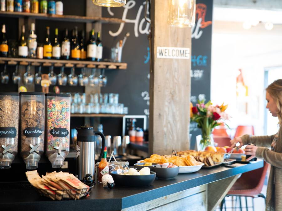Uma área de bar com diversos alimentos e uma atendente.
