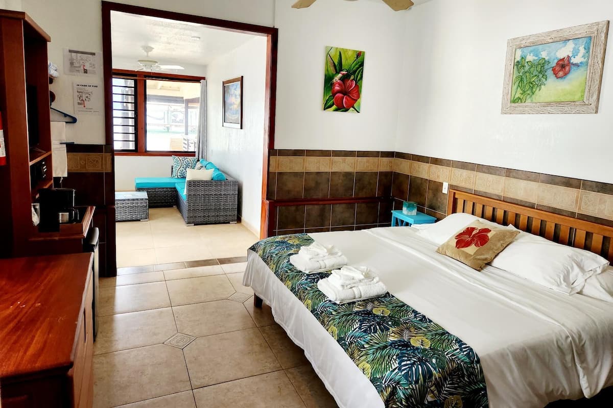 Quarto de hotel com cama, escrivaninha, cadeira, mesa pequena e ventoinha no teto.