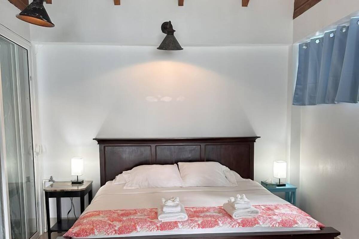 Quarto com cama de madeira, ventoinha no teto e mesa de cabeceira com abajur.
