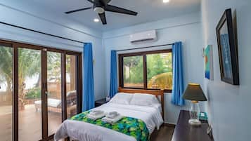 Quarto com cama, ventilador de teto, ar condicionado, mesa de cabeceira, abajur e vista para o exterior.