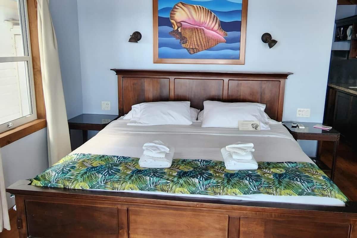 Quarto com cama de madeira, ventilador de teto, pintura de uma concha e mesa de cabeceira de madeira.